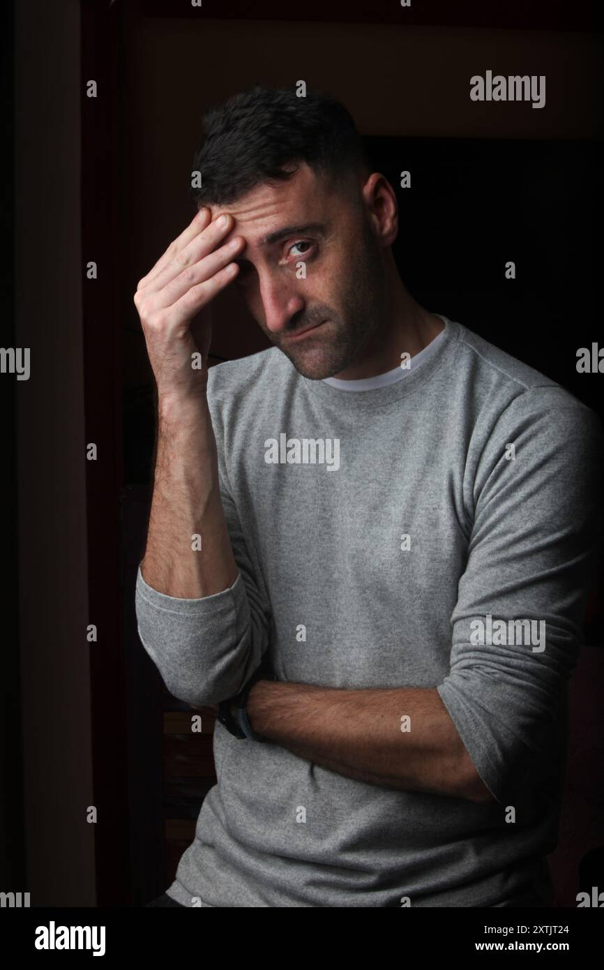 portrait of a puzzled hispanic man in low lighting on black background ...