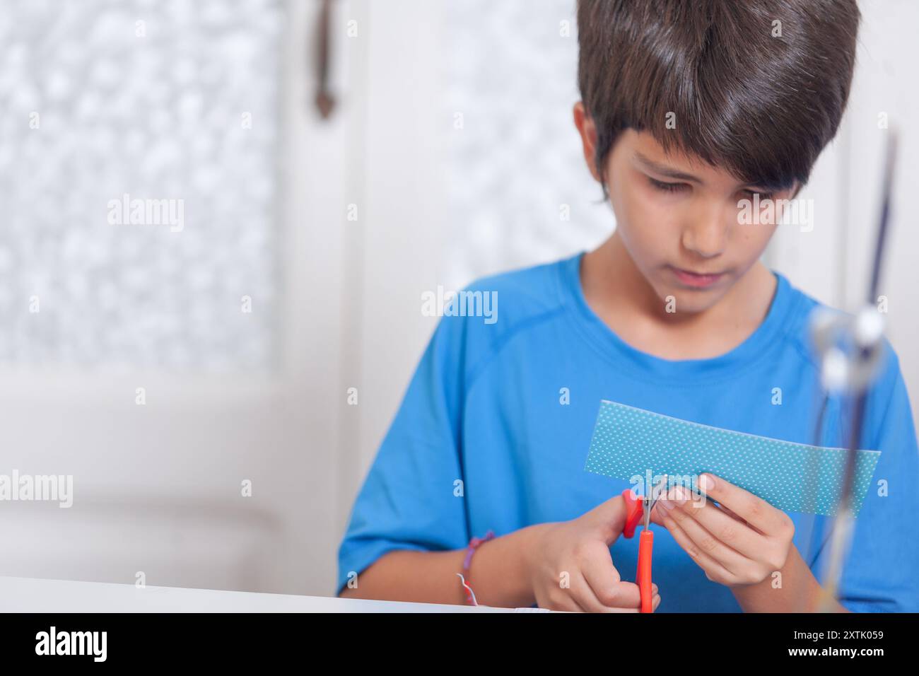 Boy cuts out blue patterned paper with red scissors. Education and ...