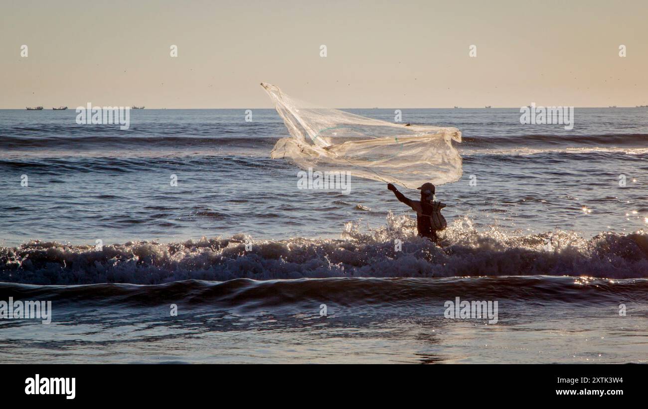 A fisherman throws his net in the surf on the beach in Cox's Bazar in ...