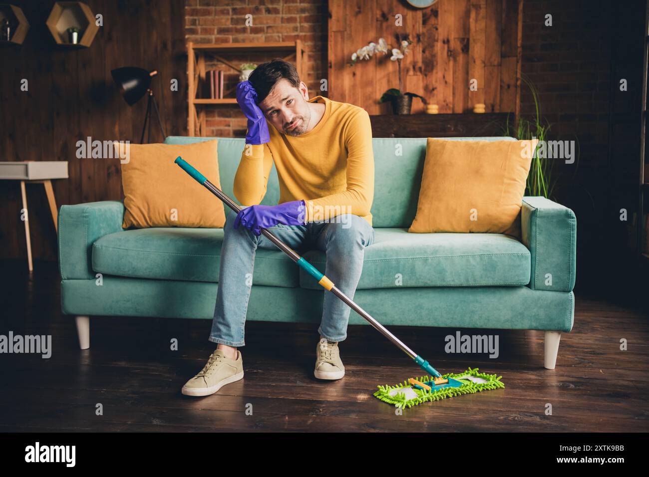 Full length photo of young guy mopping floor clean house sit couch ...