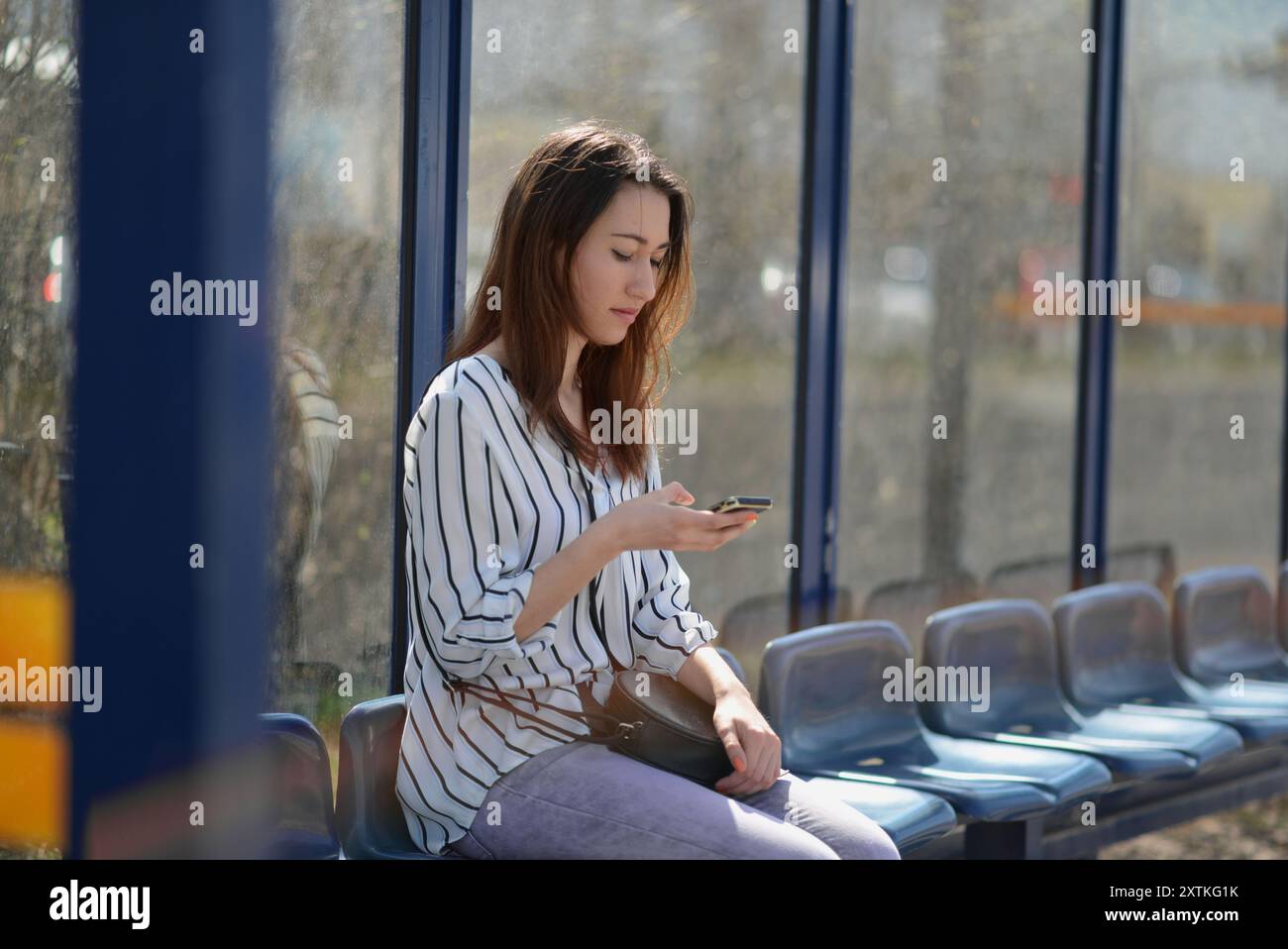A girl sits alone at a bus stop using a mobile phone Stock Photo - Alamy