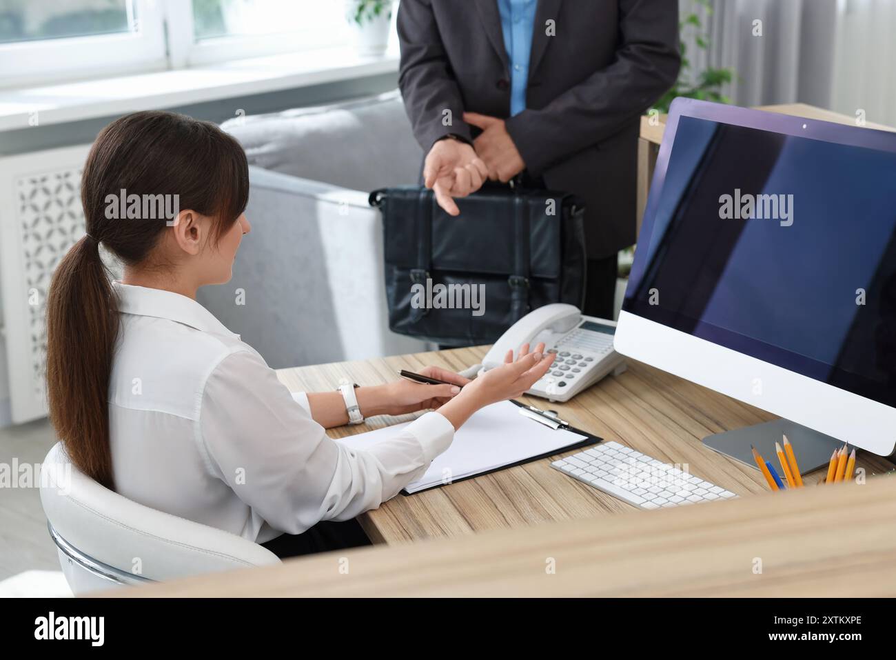 Professional receptionist working with client in office Stock Photo - Alamy