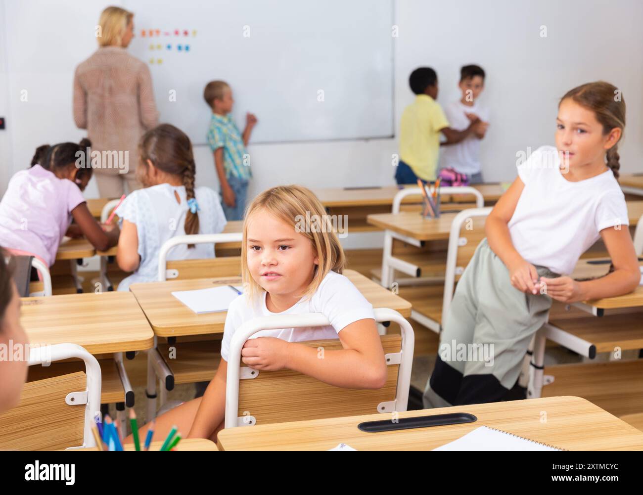 Happy preteen schoolchildren communicating during recess in classroom ...