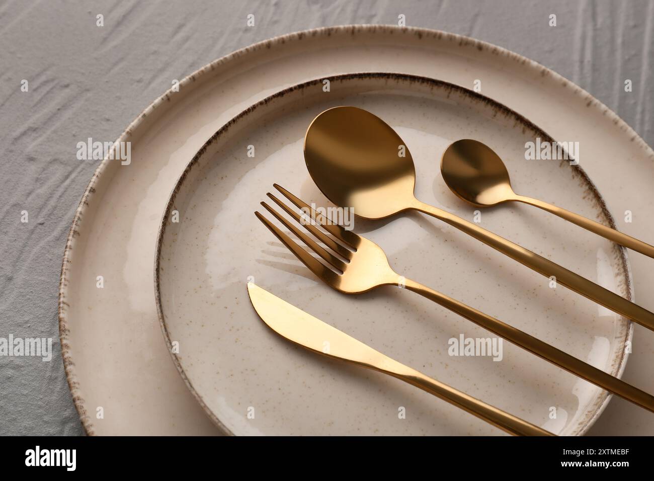Golden set of cutlery with beige plates on grey background Stock Photo ...