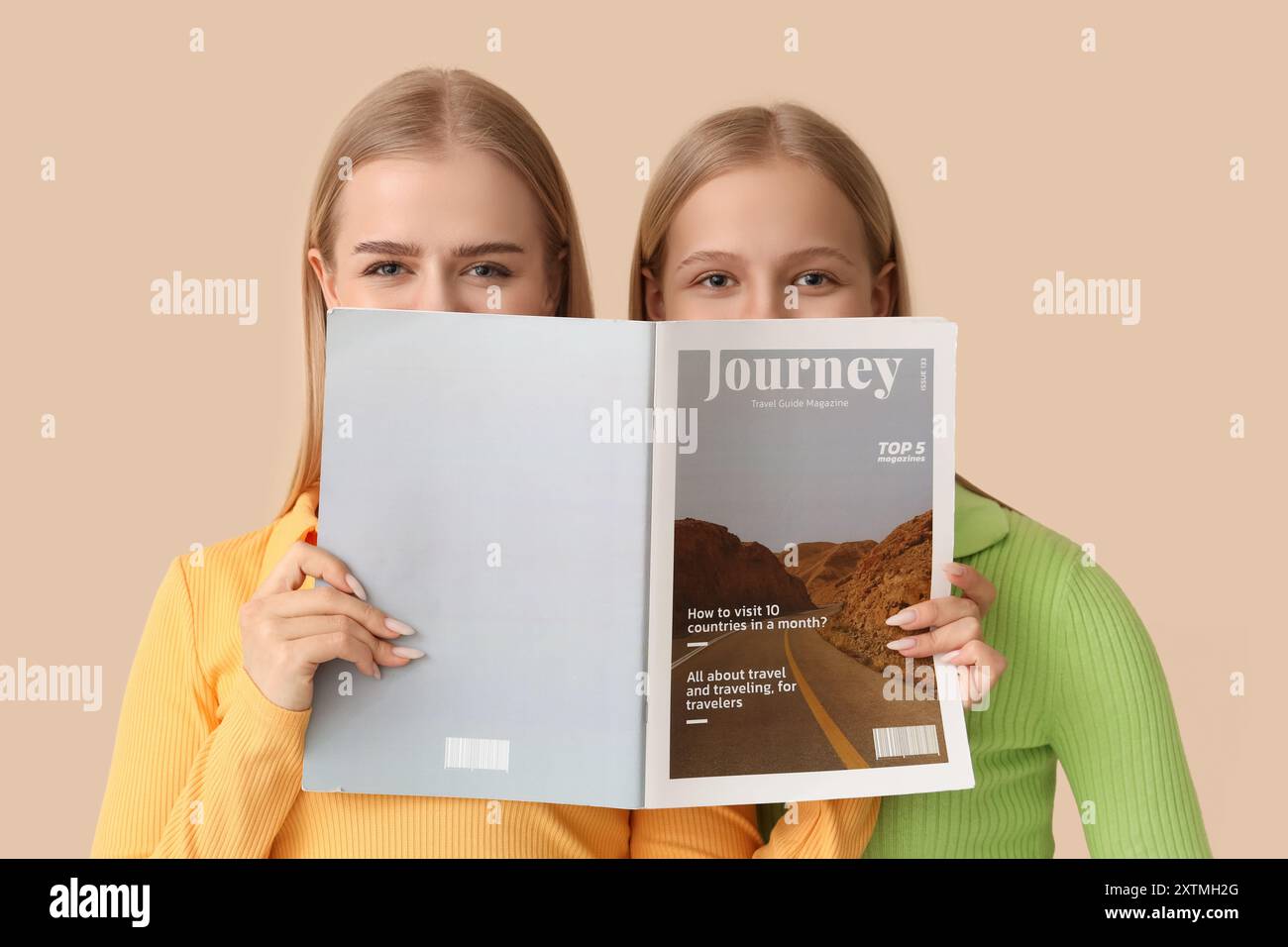 Beautiful young sisters hiding behind open magazine on beige background ...