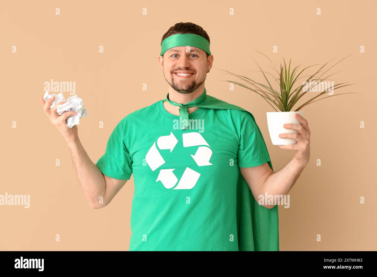 Young man dressed as eco superhero with houseplant and rubbish on beige ...