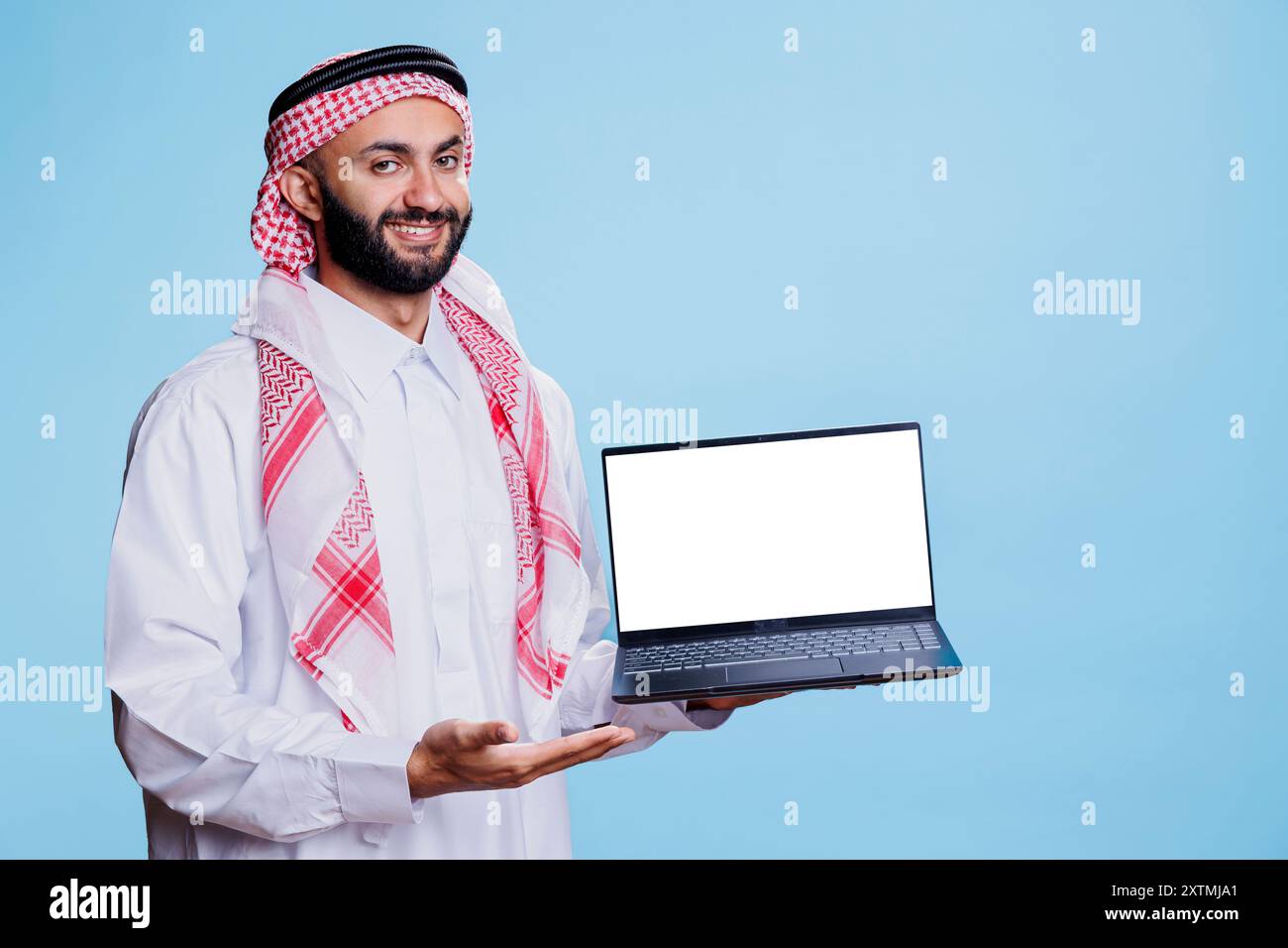 Smiling muslim man holding laptop and pointing with hand at empty white ...