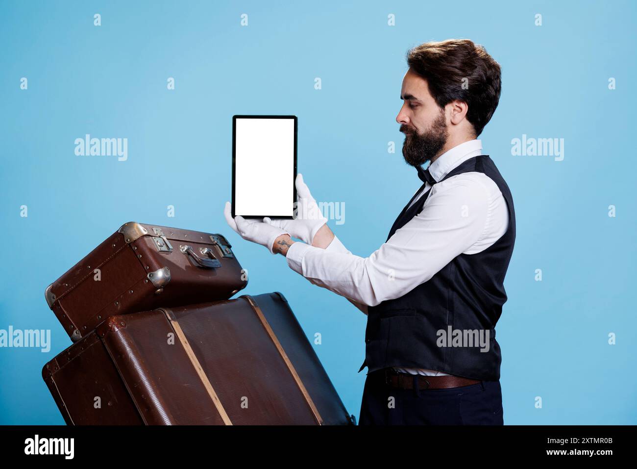 Classy bellhop presenting tablet on camera and showing isolated white ...