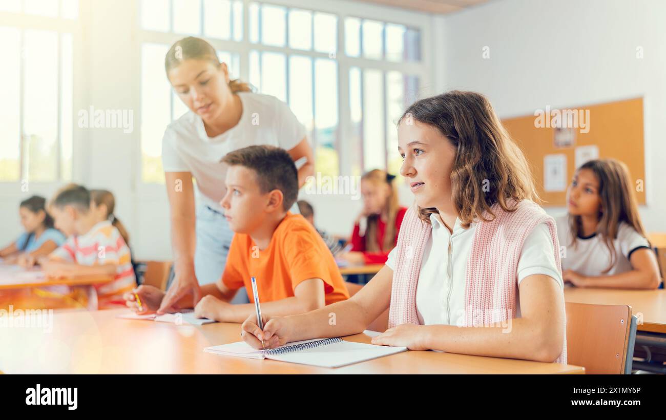 Assiduous focused tween girl sitting with pen and notebook at lesson ...