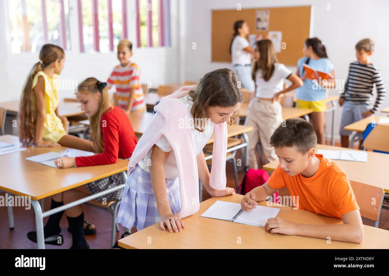 Tween girl helping classmate to complete written assignment in class ...