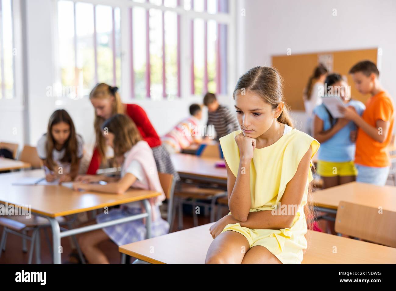 Sad bored girl sitting separately in classroom in break between lessons ...
