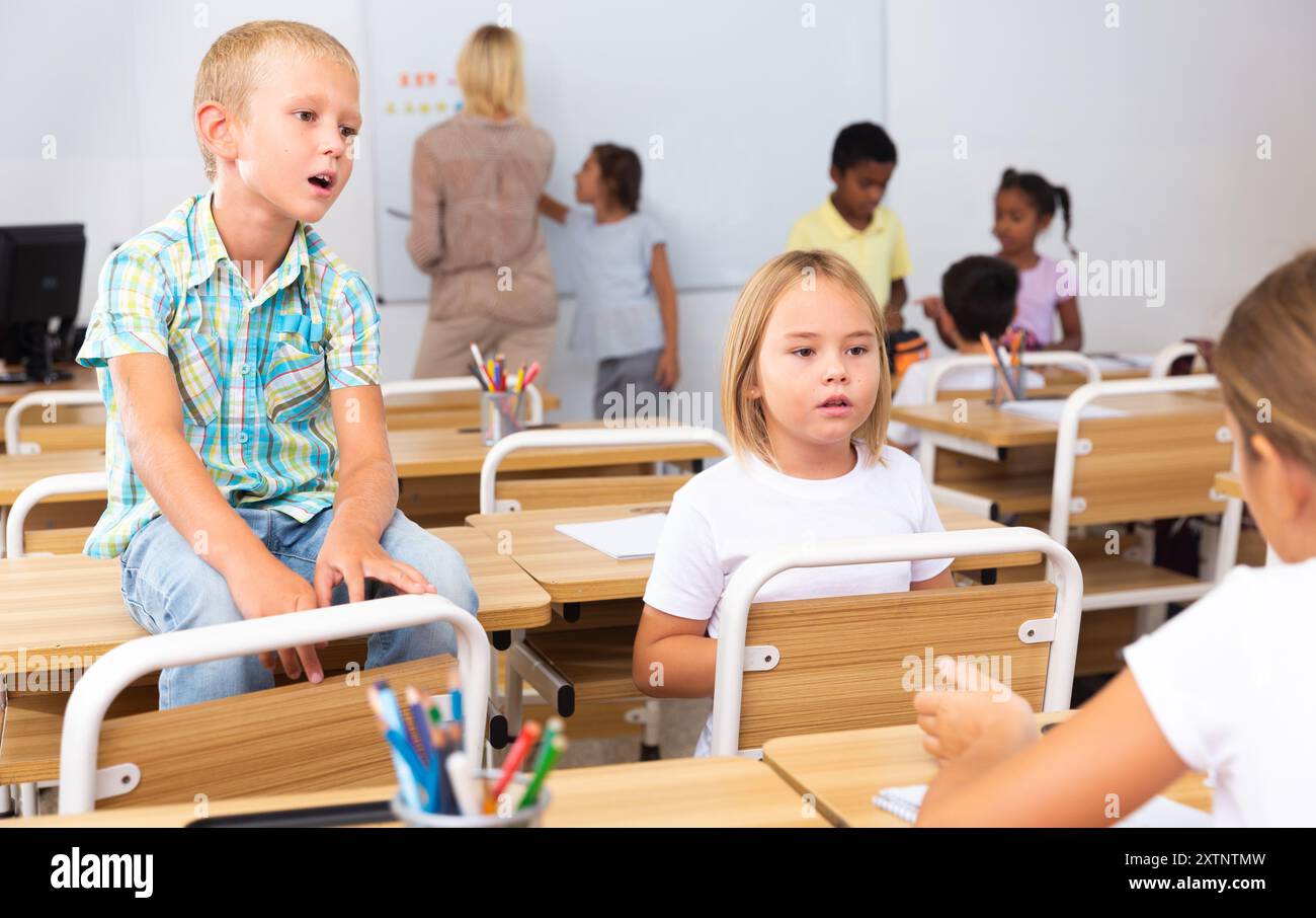 Happy preteen schoolchildren communicating during recess in classroom ...