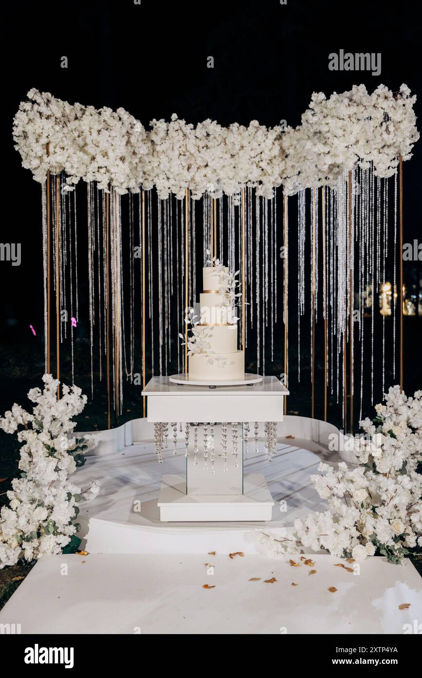 Wedding setup with three-tier white cake with floral accents. Wedding ...