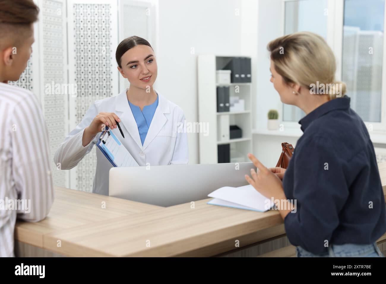 Professional receptionist working with patients at wooden desk in ...