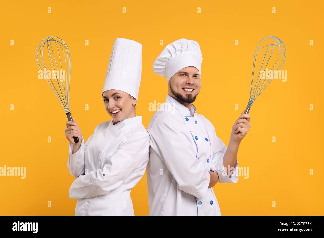 Happy pastry chefs with big whisks on orange background Stock Photo - Alamy