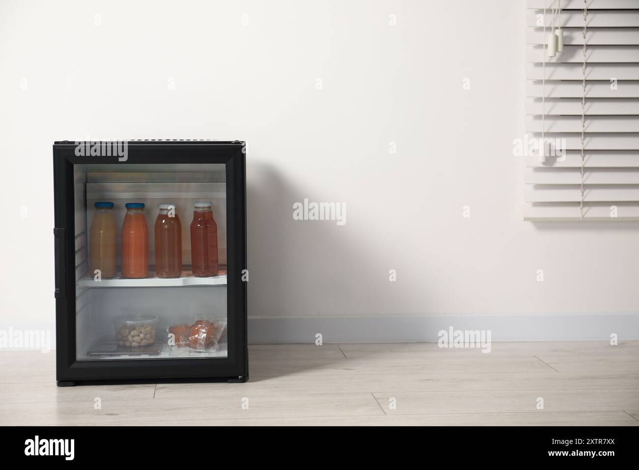 Mini refrigerator with different drinks and snacks near white wall ...