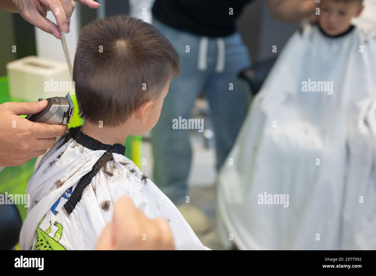 A scene from the back as a barber trims a young boy's hair while he ...