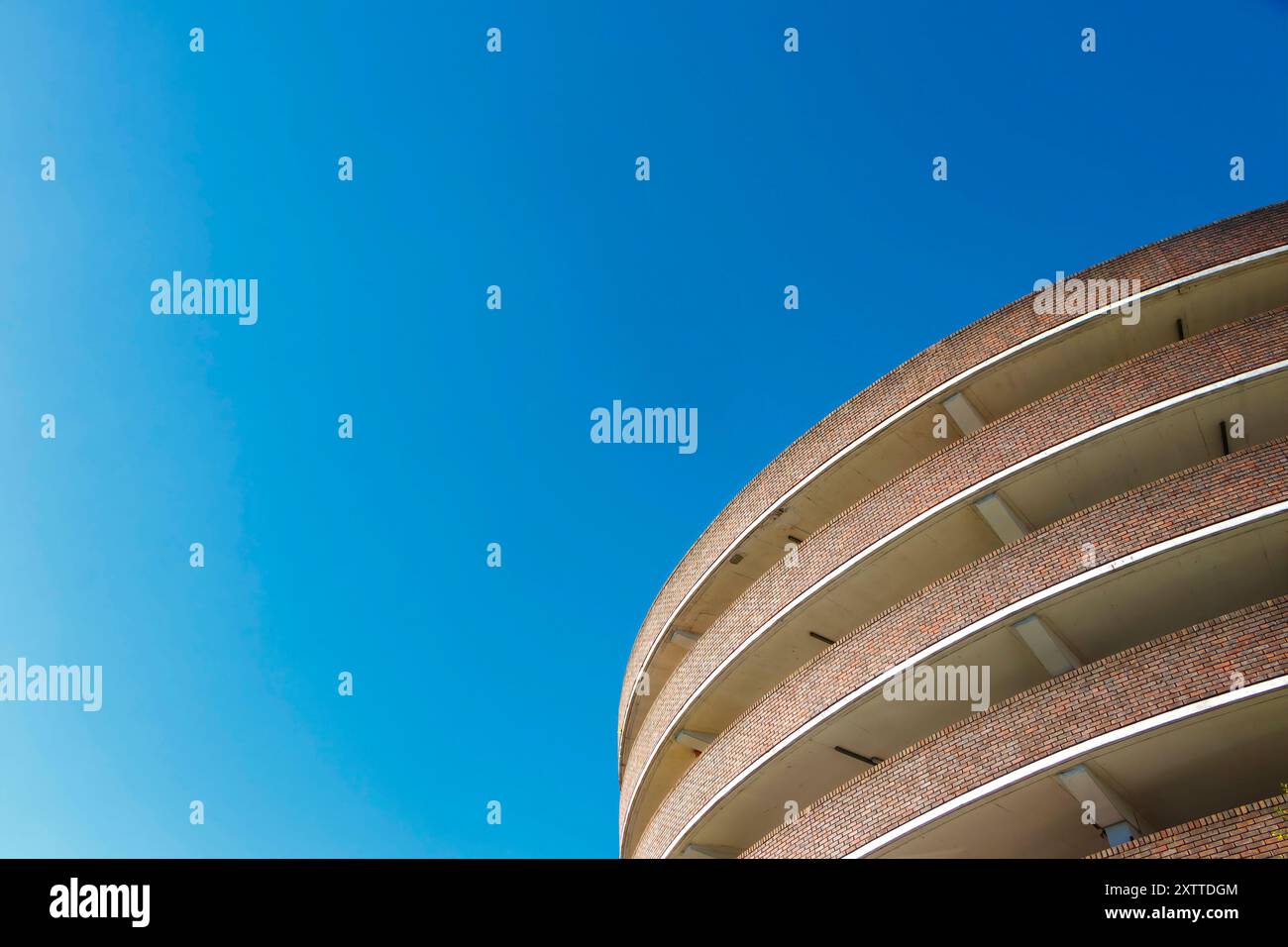 Curved multi-story brick parking garage with a clear blue sky as ...
