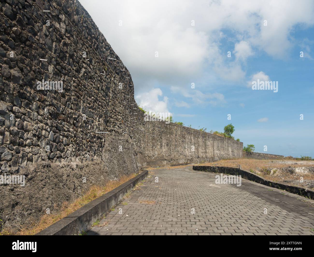 Large stone wall positioned alongside path with grey brick paving in ...