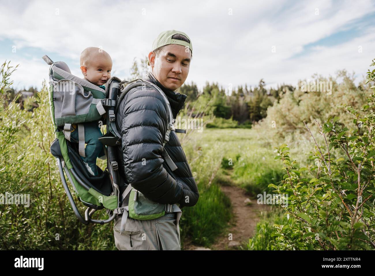 Asain dad with backpack looking at smiling baby in lush countryside ...