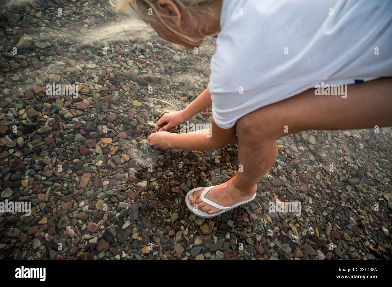 Child washing rocks in the crystal-clear waters of a mountain lake ...
