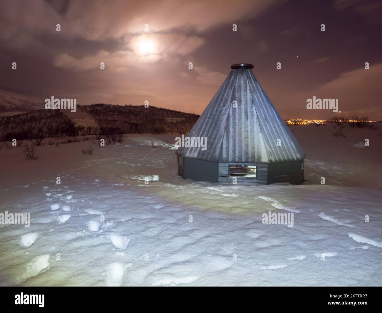 Wooden cabin in Northern Norway in winter. Visible lights inside. Gate ...