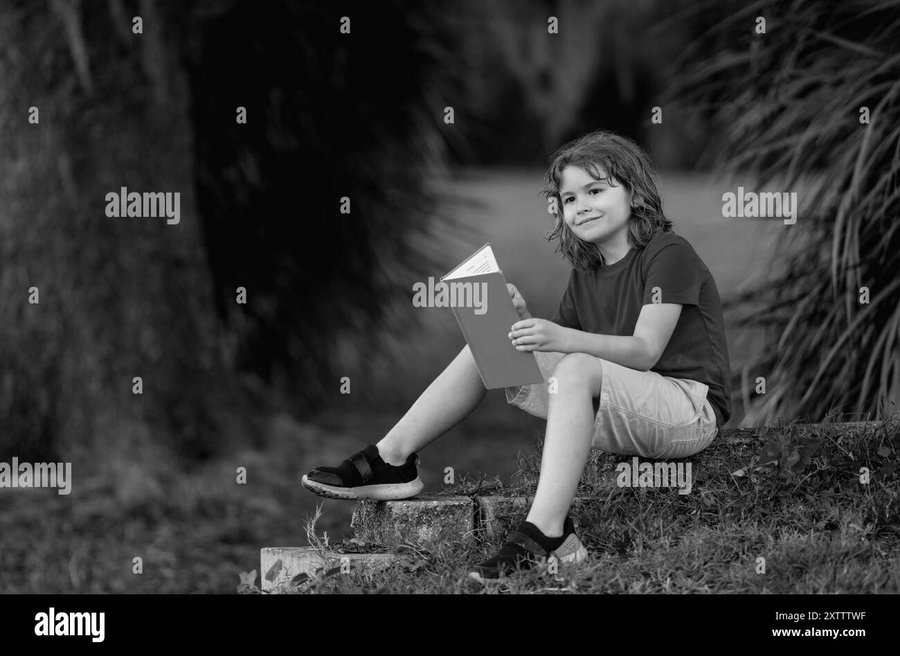 Cute little boy reading book in park. Kid sit on grass and reading book ...