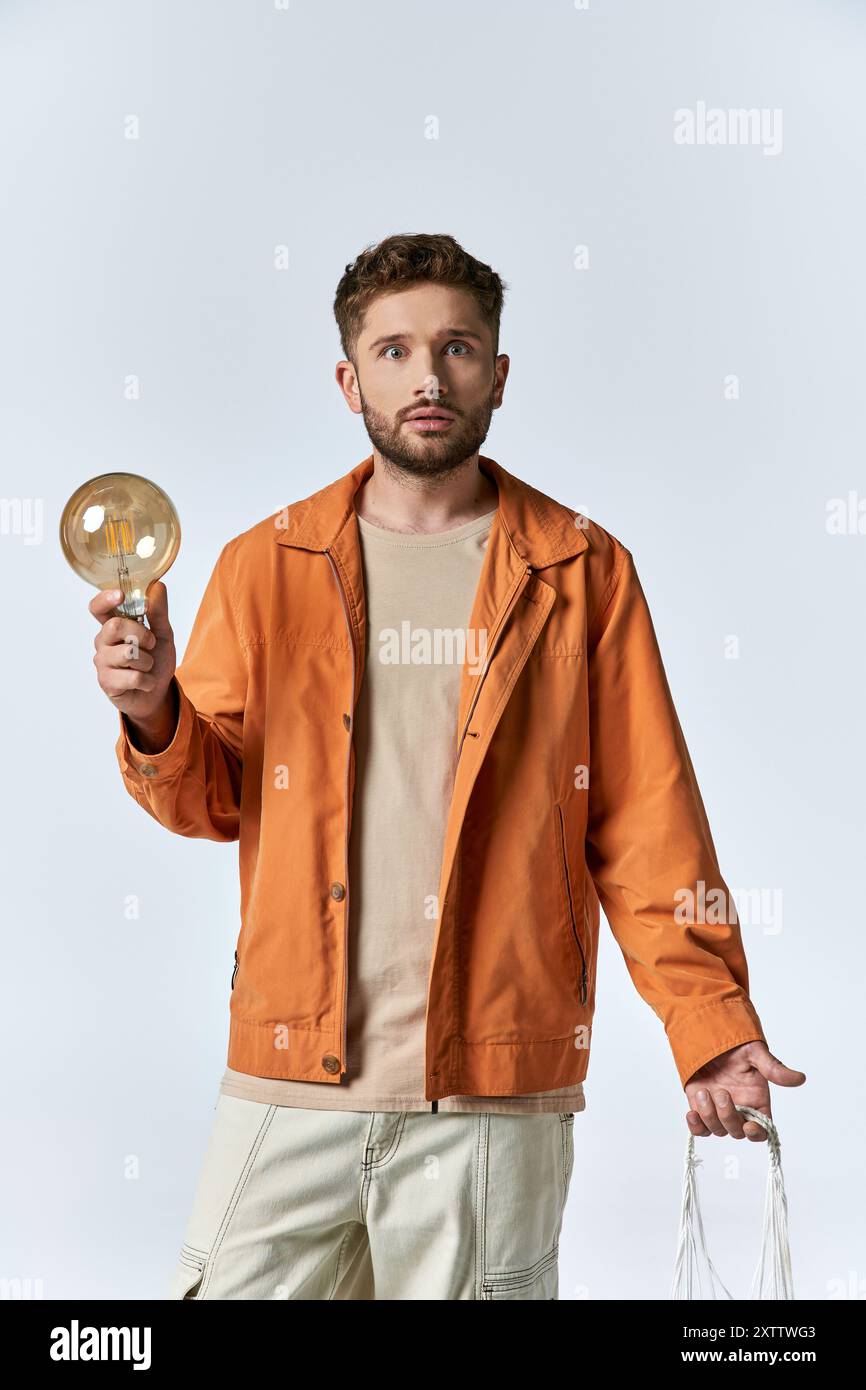 A man in an orange jacket holds a lightbulb and stares intently Stock ...