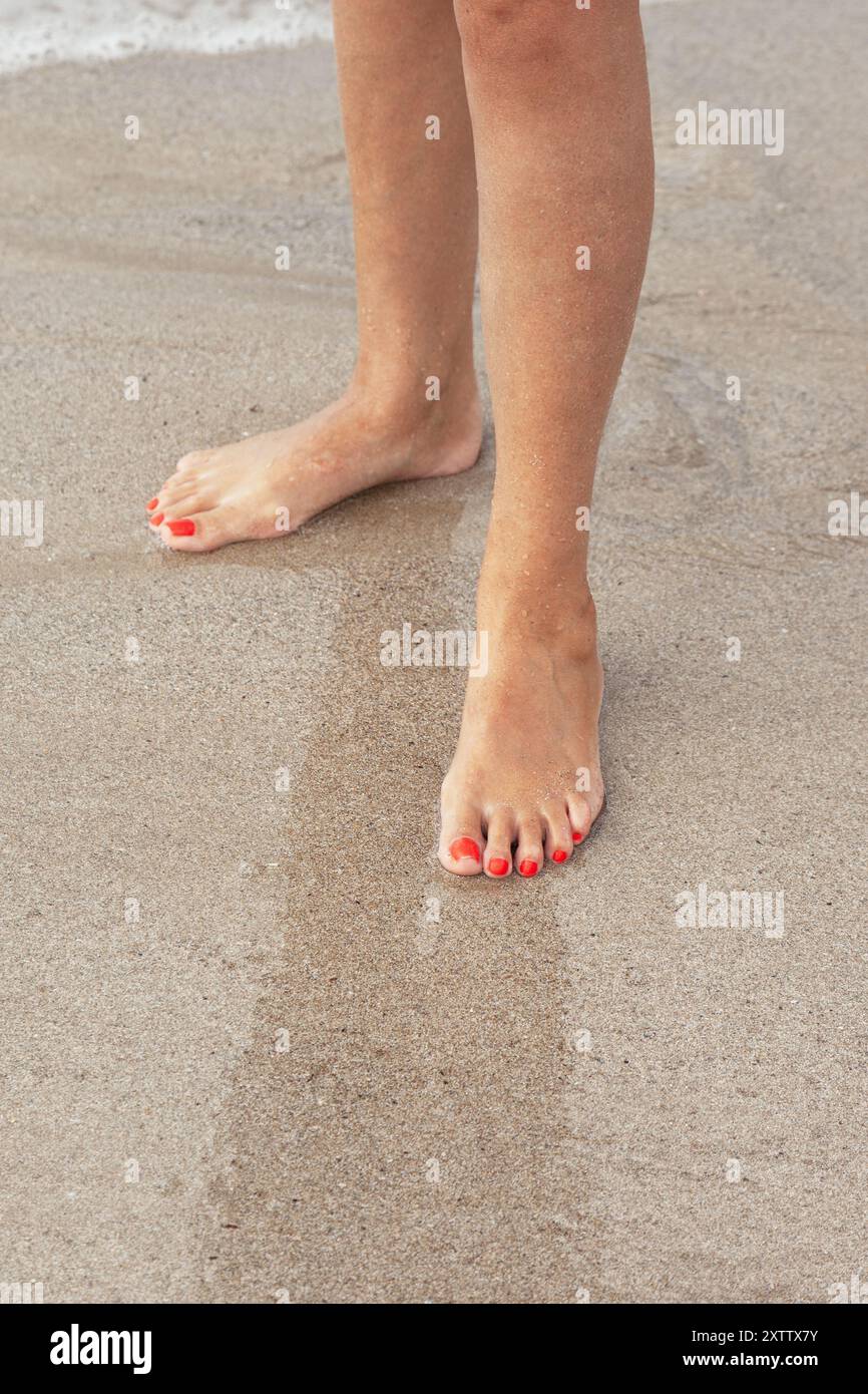 Female feet on beach sand. Woman's feet with red nails on seashore sand ...