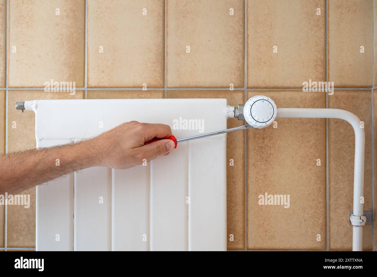 Caucasian male hand with a screwdriver fixing the thermostat on a home ...