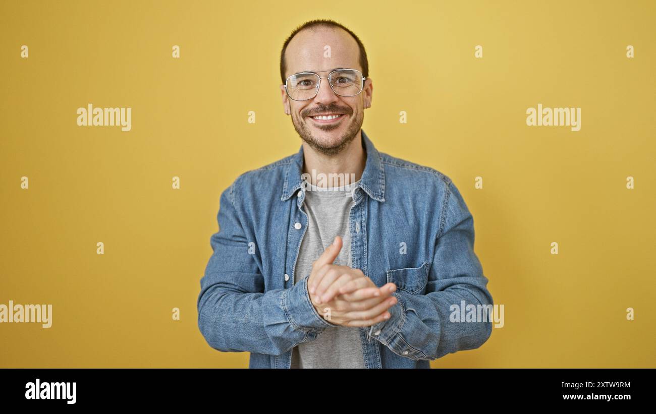 A cheerful bald man with a beard clapping hands in front of a yellow ...
