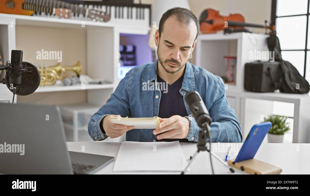 Hispanic bald man with beard in studio using microphone and laptop for ...