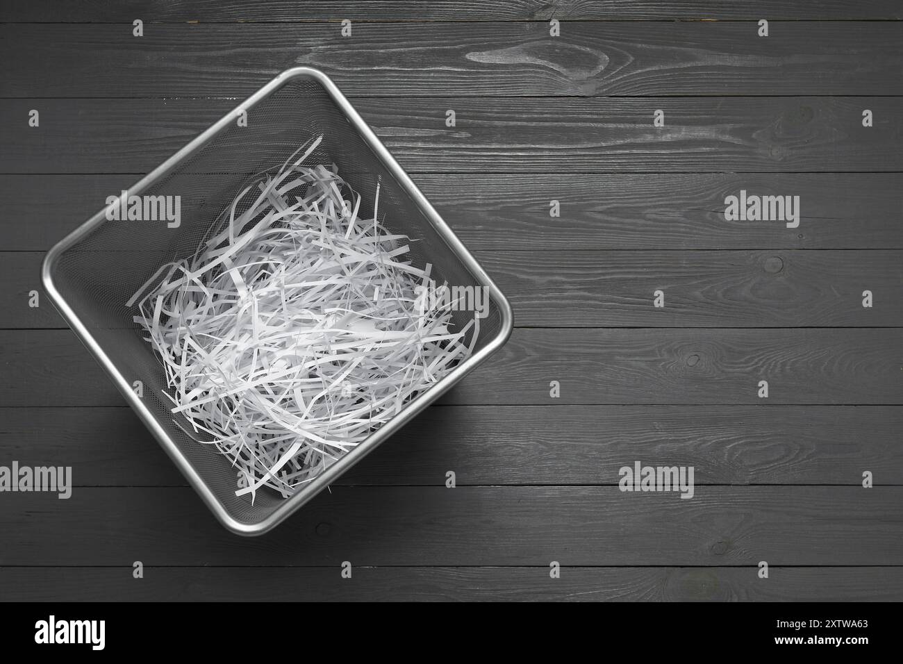 Shredded paper strips in trash bin on grey wooden table, top view ...