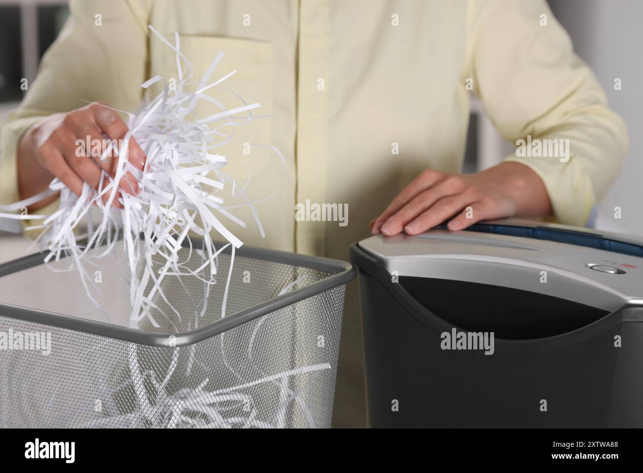 Woman putting shredded paper strips into trash bin indoors, closeup ...