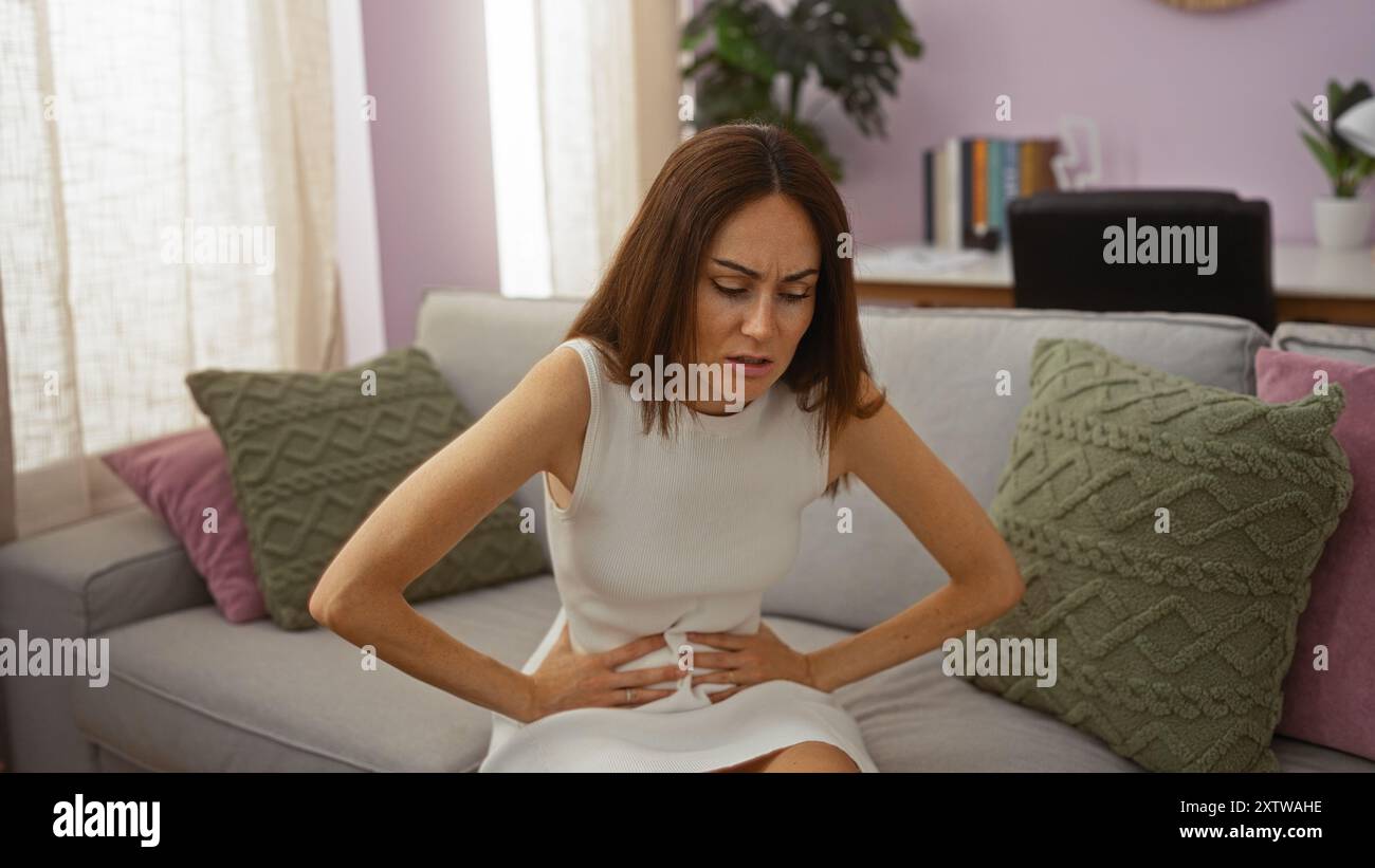 Woman suffering abdominal pain sitting on a cozy couch in a living room ...