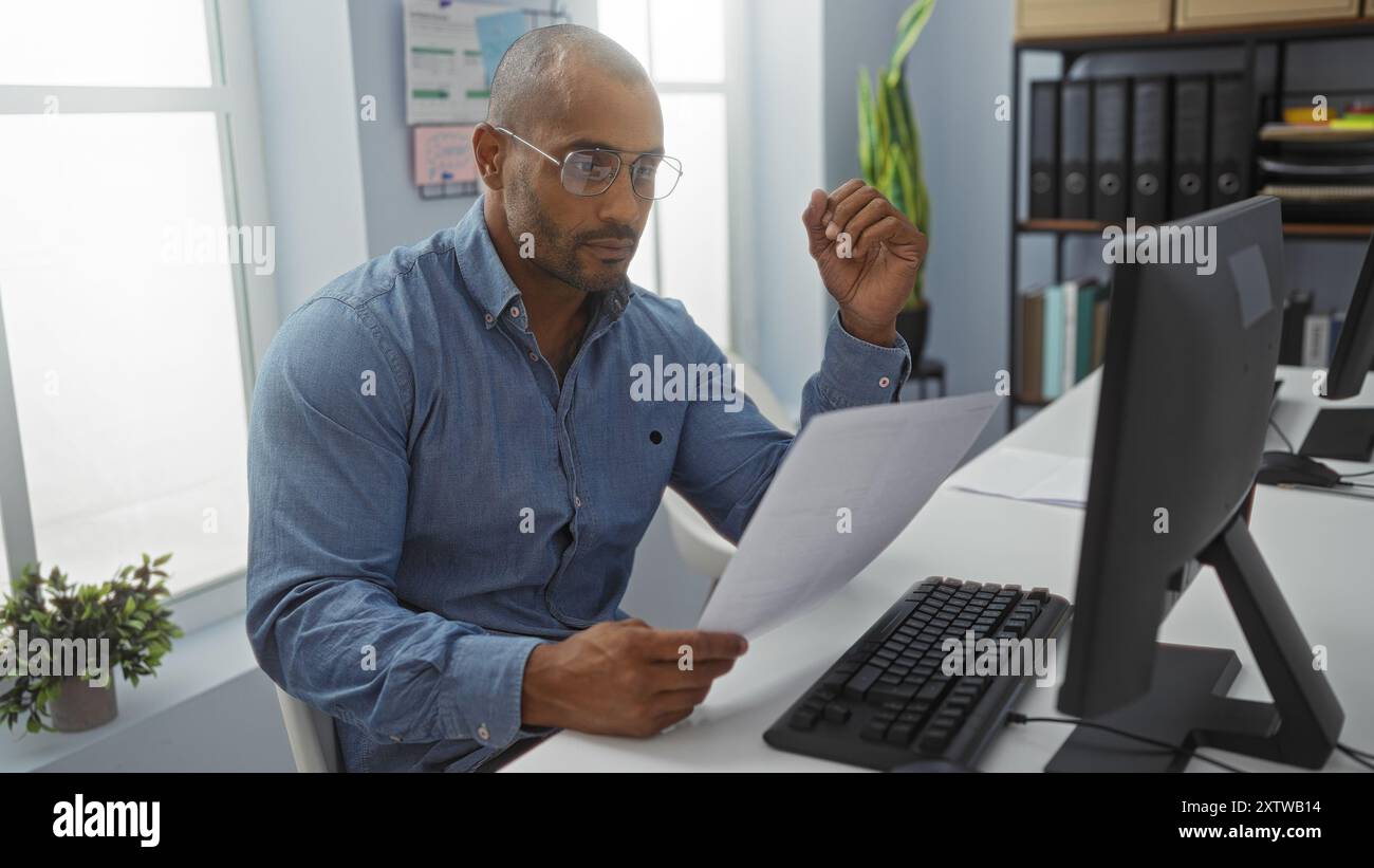 Young black man working in an office, focused on a document, with a ...