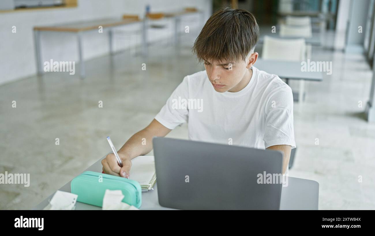 A focused young man studying with pen and laptop at a table in a modern ...