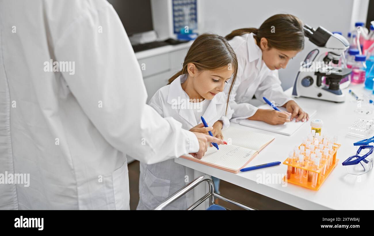 Two young girls in lab coats taking notes in a science laboratory with ...