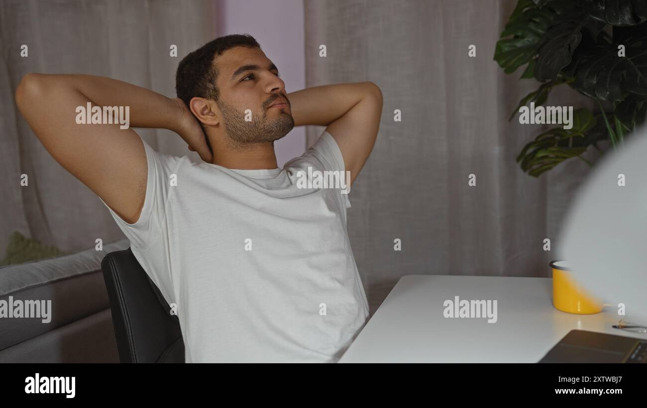 Young man relaxing indoors at home, leaning back in a chair with hands ...