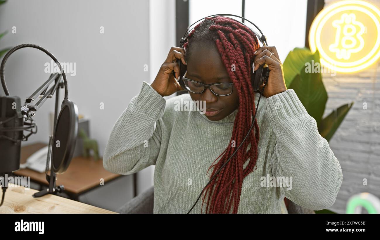 African woman with braids adjusting headphones indoors at a podcasting ...