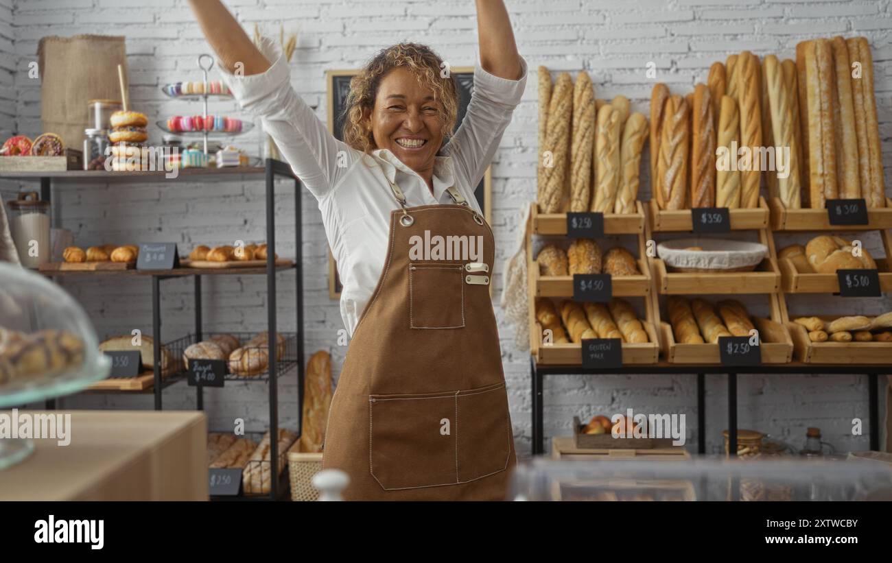 Middle-aged woman raising arms in celebration inside a bakery filled ...