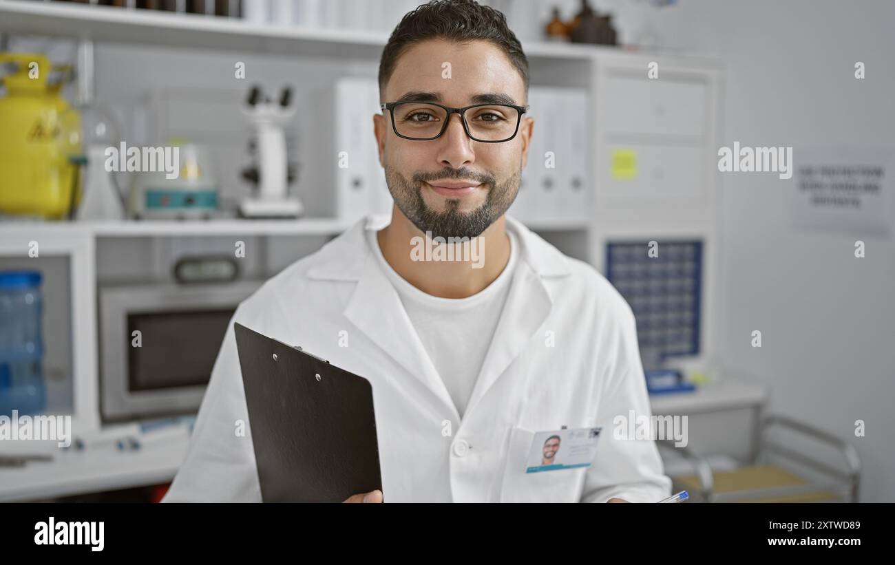 A confident young man with a beard, wearing glasses and a lab coat, holding a clipboard in a ...