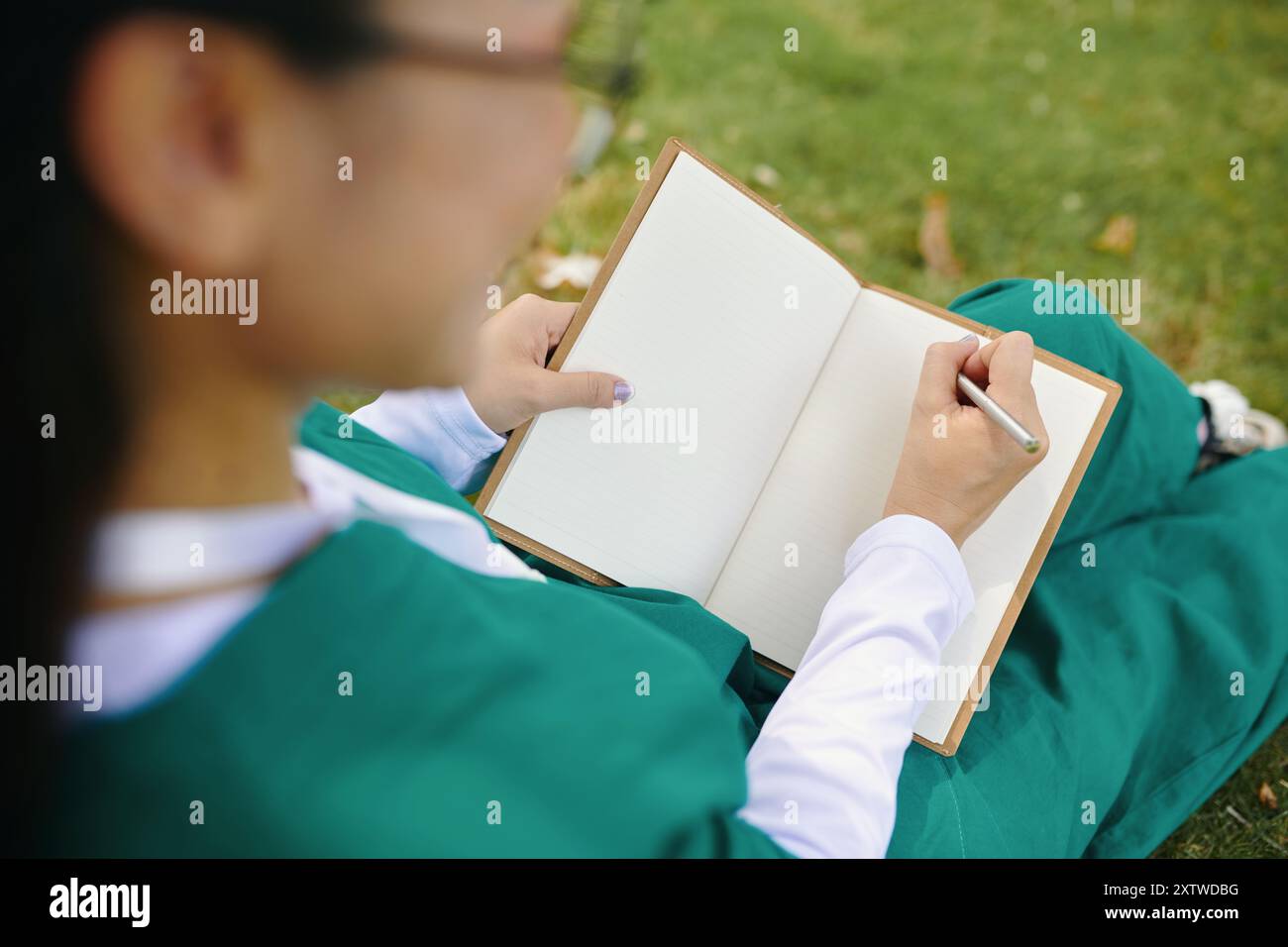 Person Writing in Notebook on Lawn in Green Attire Stock Photo - Alamy