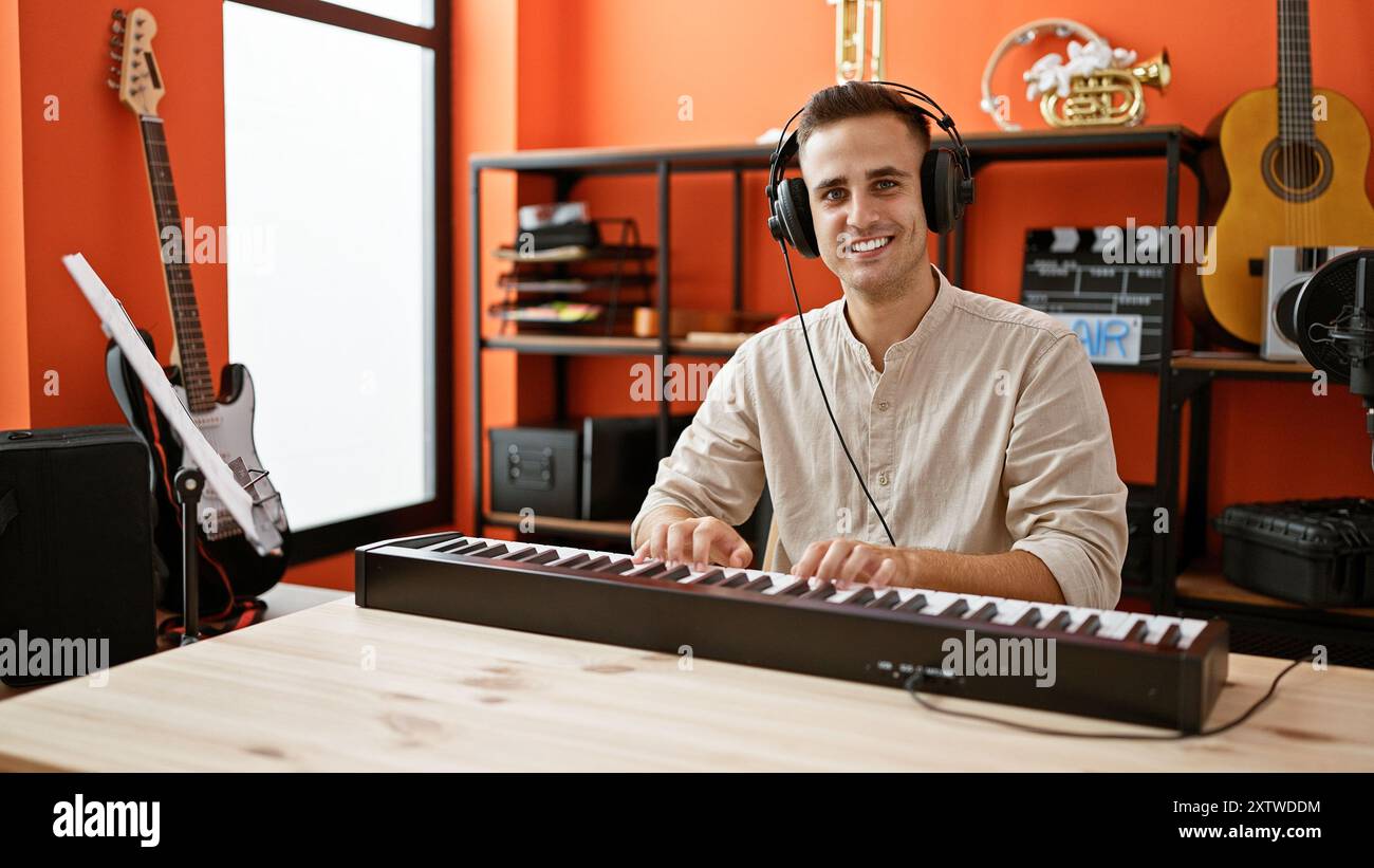 Smiling young man playing keyboard in a music studio with guitars and ...