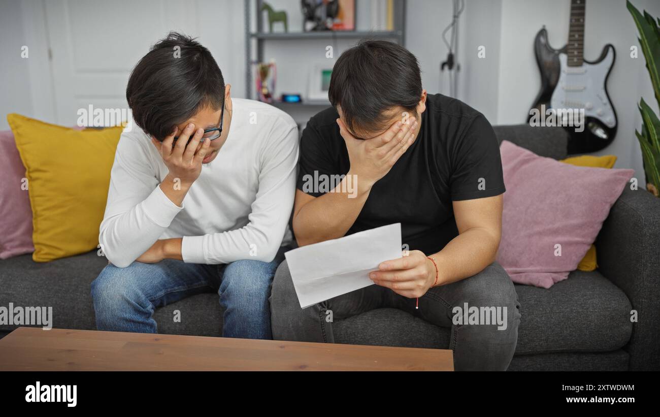 Two distressed asian men reviewing a document together on a couch in a ...