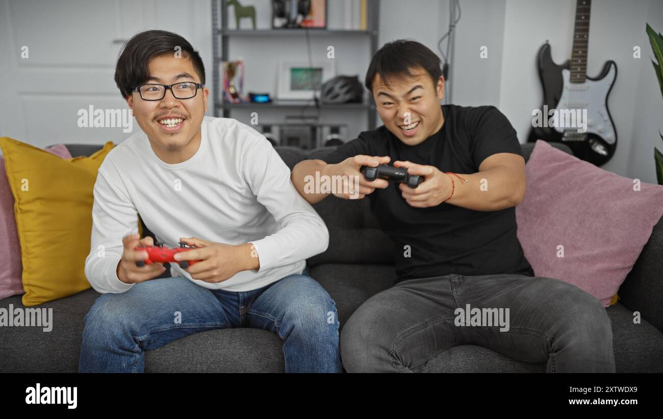 Two asian friends competing happily in a video game, sitting in a ...