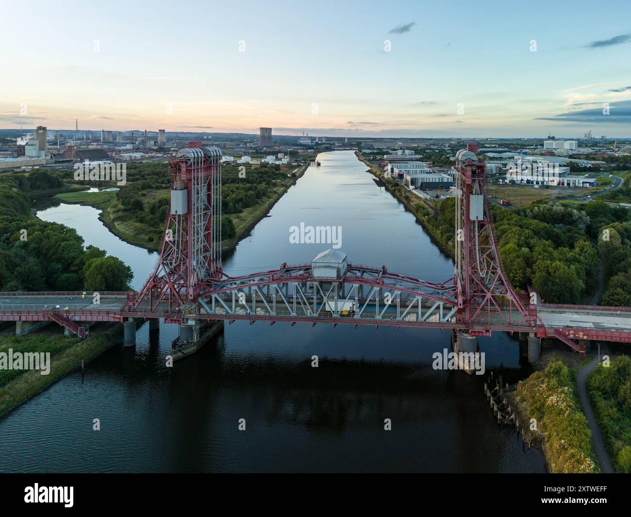 Aerial view of a red vertical-lift bridge over a river at sunset ...