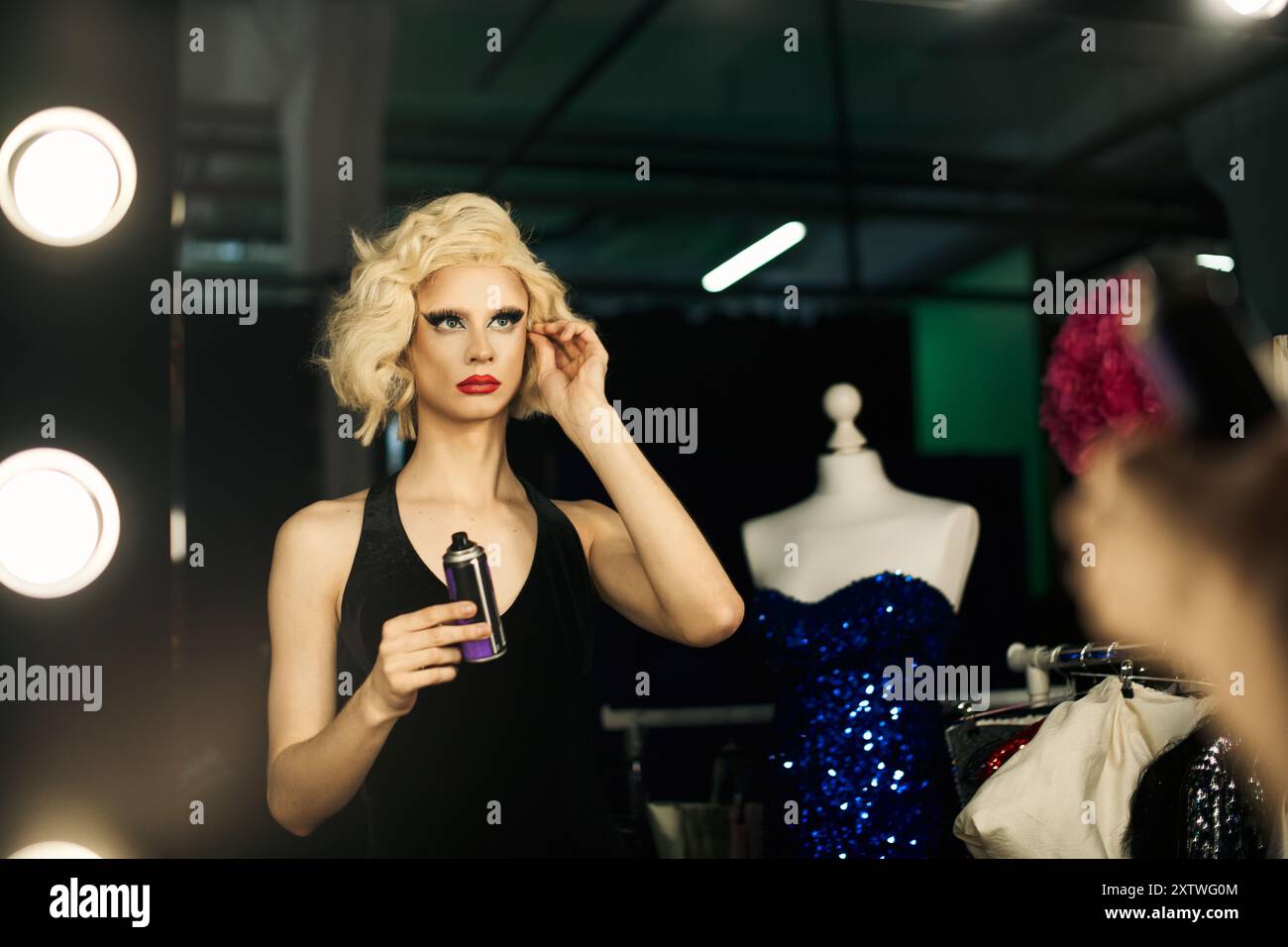 A drag queen in a black dress prepares backstage, fixing her hair with ...
