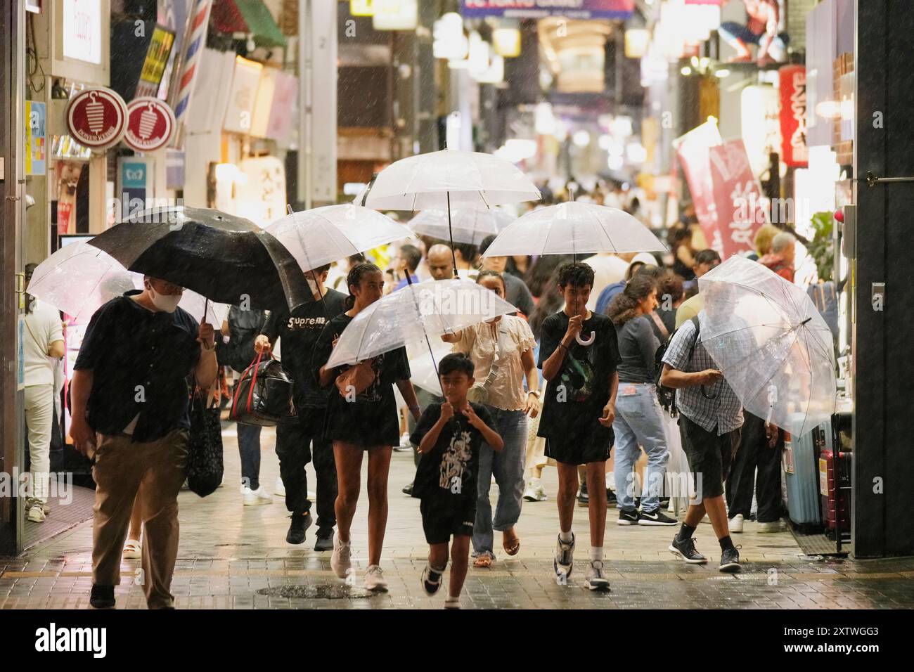 People use umbrellas as they walk through a shopping street and cross a ...