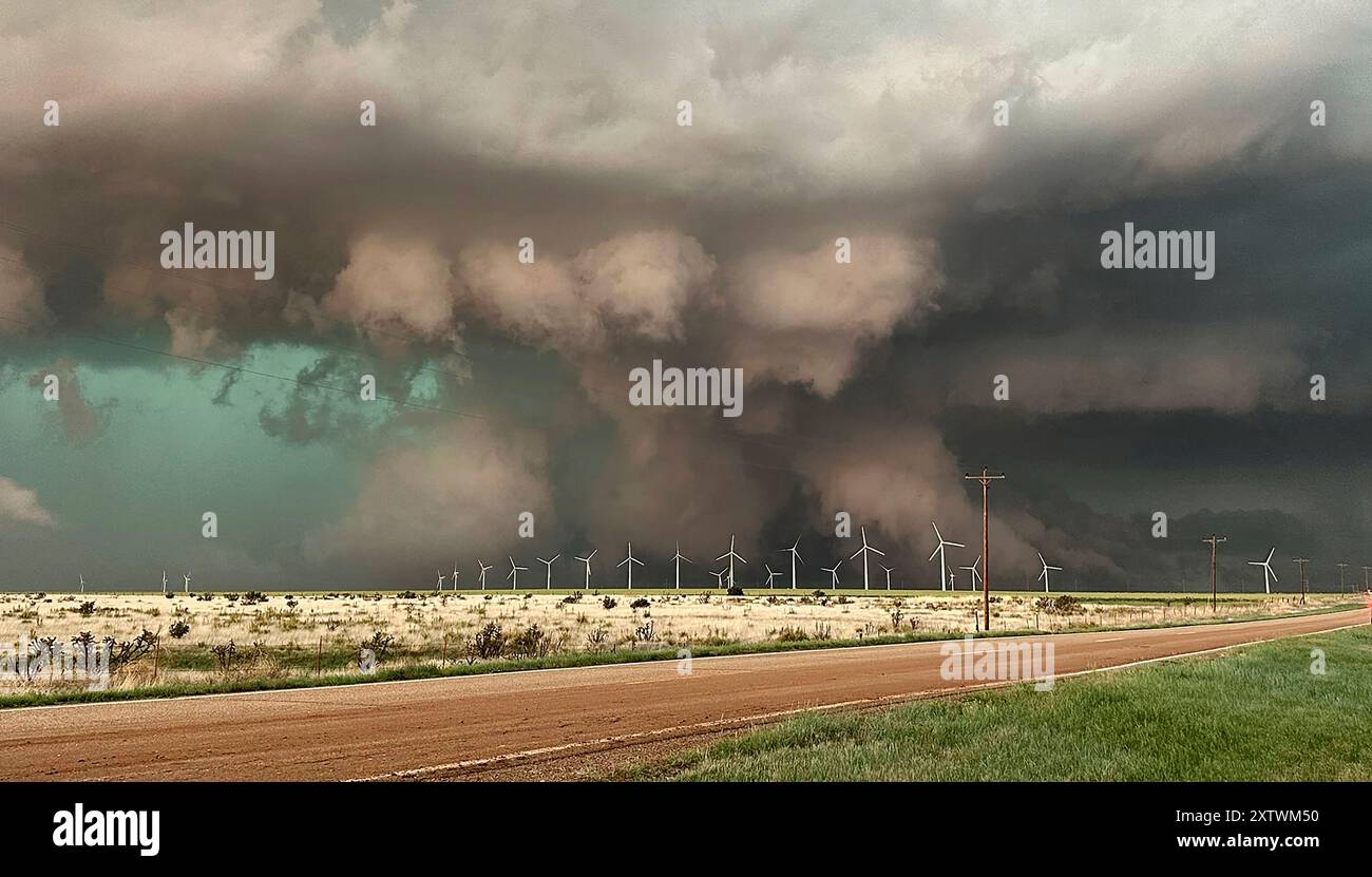 A menacing tornado forms over a wind farm with dark storm clouds ...